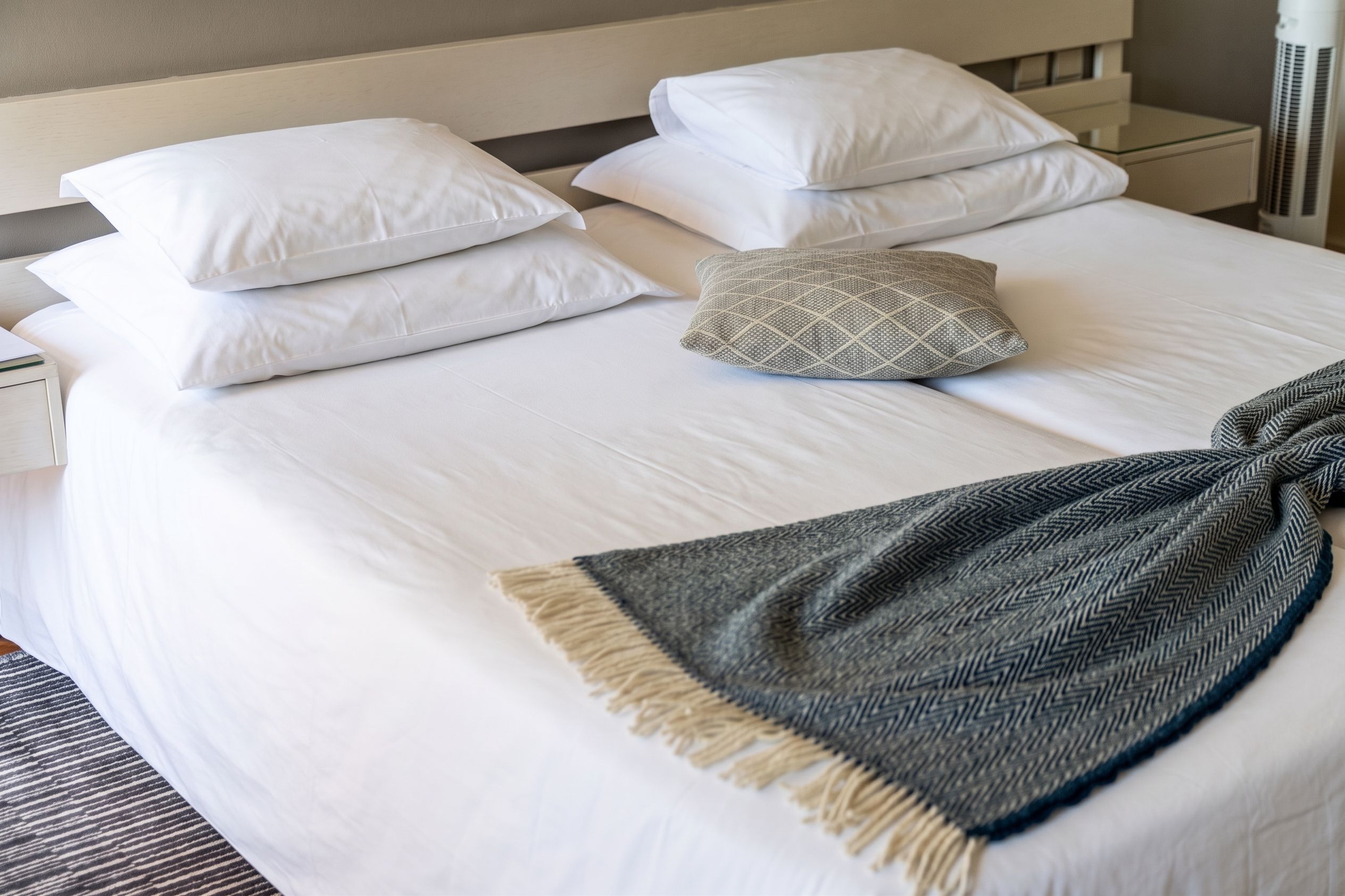 Cama bem arrumada com lençóis brancos e um cobertor cinza estampado.