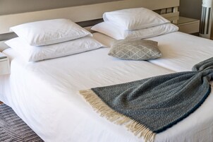 Cama bem arrumada com lençóis brancos e um cobertor cinza estampado.