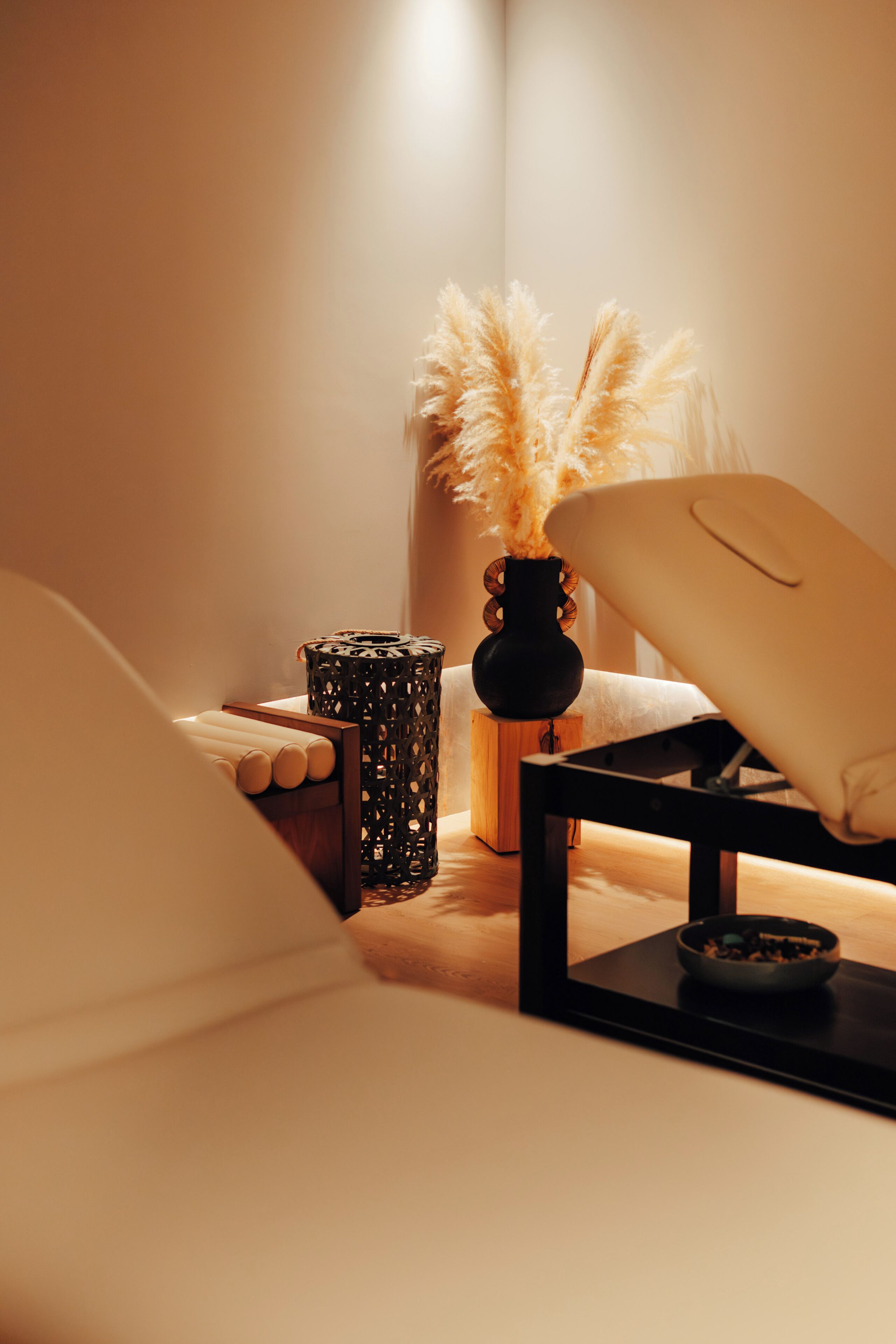 Quarto bem organizado com cama, mesa de cabeceira com um vaso de plantas secas, um recipiente decorativo e uma luminária.
