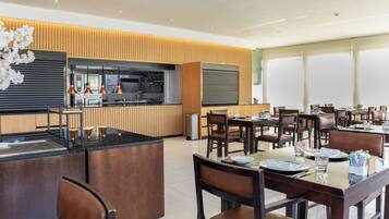 Restaurante moderno com ilha central, painéis de madeira e área de cozinha.