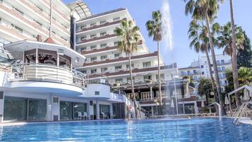 Hotel com piscina, palmeiras e fonte.
