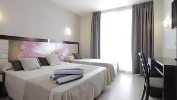 Quarto de hotel com duas camas, uma escrivaninha e uma janela grande com cortinas.