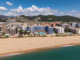 Um hotel à beira-mar com vários edifícios, uma praia e montanhas ao fundo.