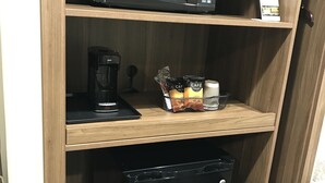 Uma estante de madeira com micro-ondas, máquina de café e lixeira.
