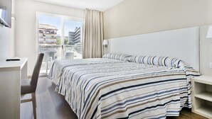 Quarto de hotel com cama, escrivaninha, cadeira e janela com cortinas.