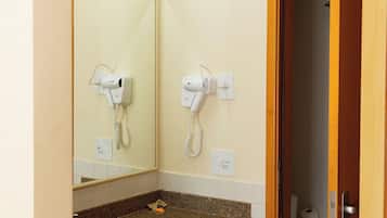 Casa de banho com bancada de granito, dois secadores de cabelo fixados na parede, um espelho e uma sanita visível através de uma porta aberta.