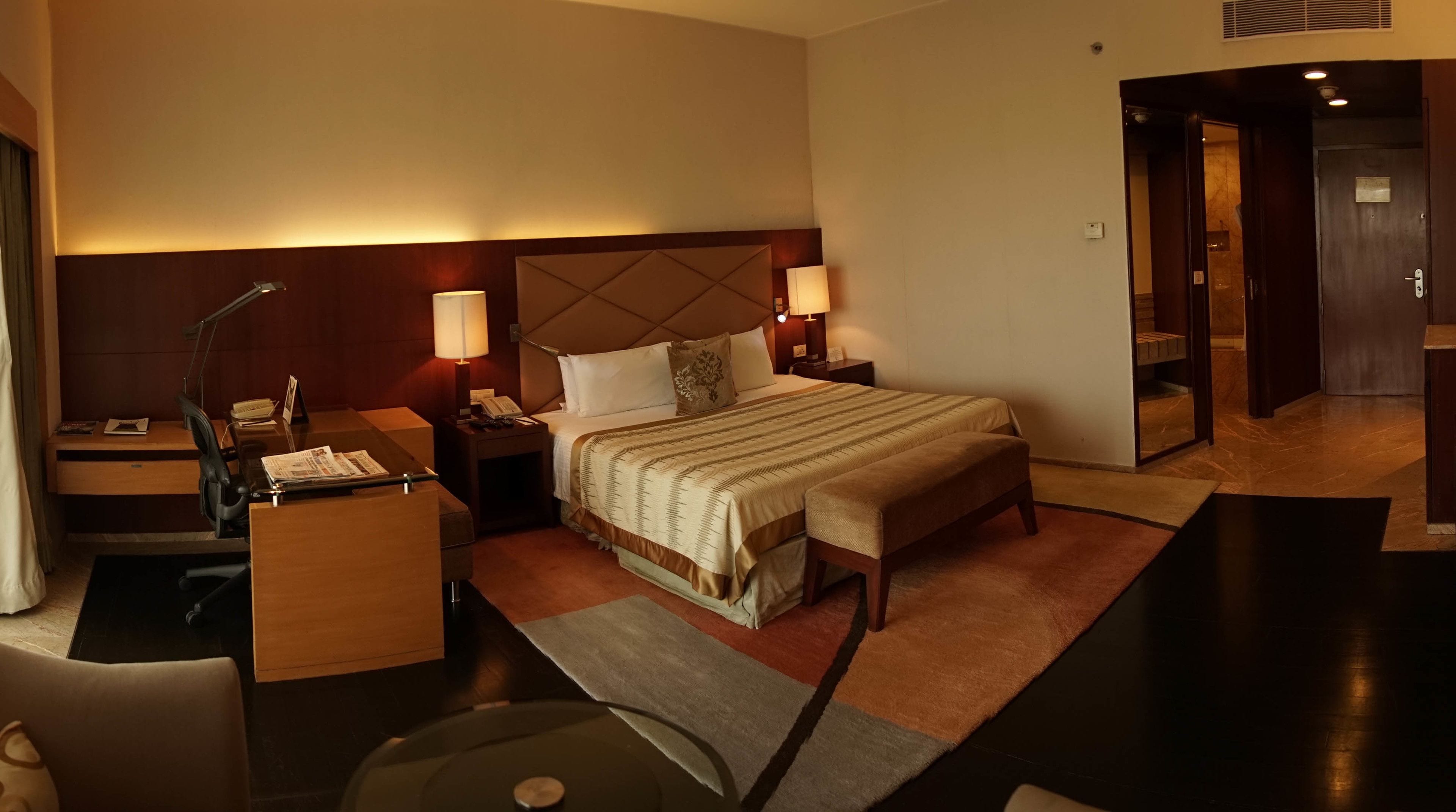Quarto de hotel com cama, escrivaninha, cadeira e abajures.