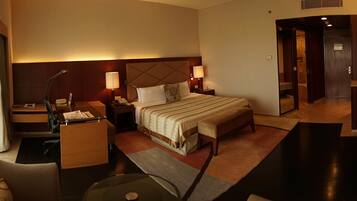 Quarto de hotel com cama, escrivaninha, cadeira e abajures.