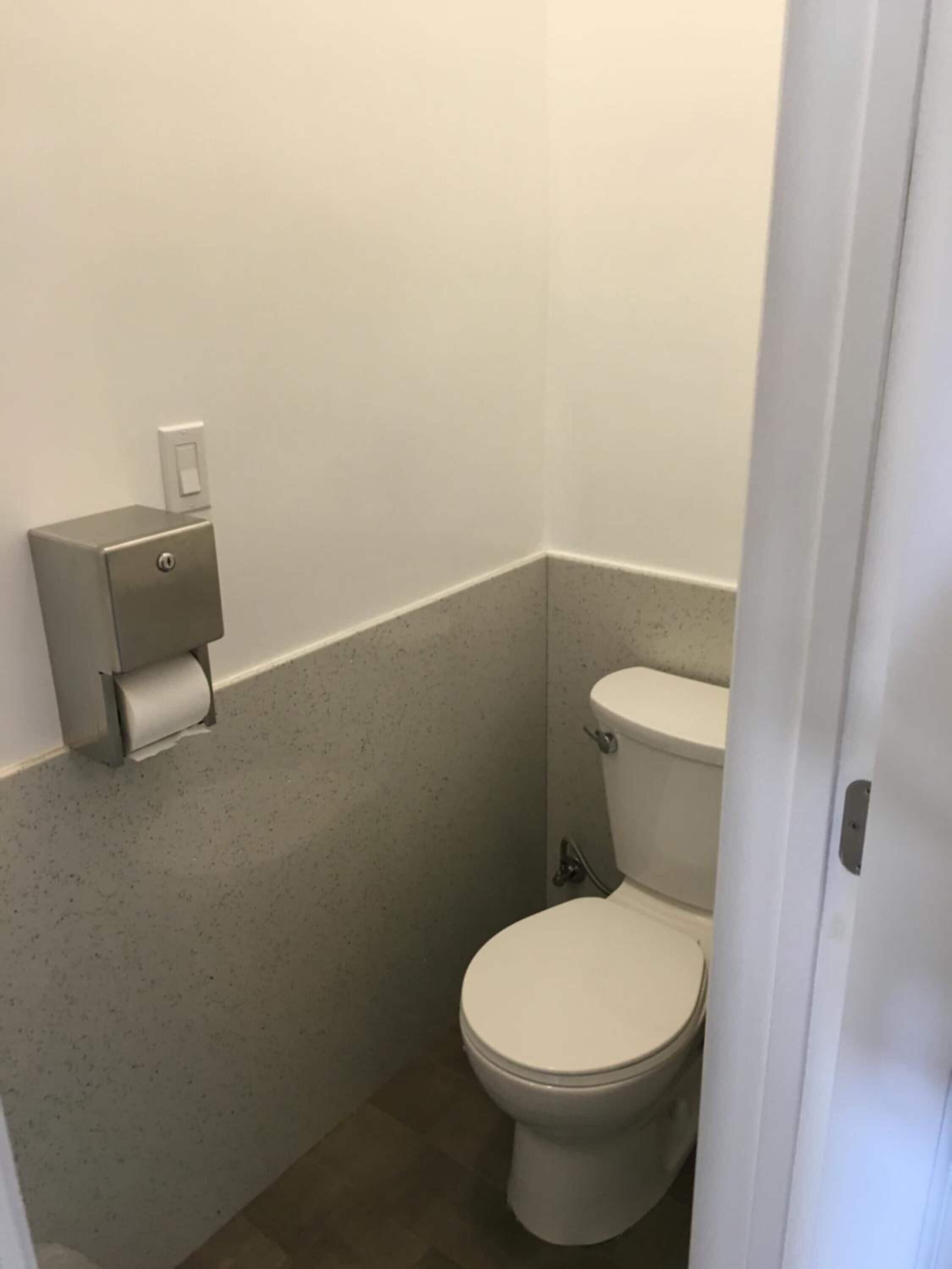 Casa de banho pequena e compacta com sanita, dispensador de papel e interruptor de luz na parede.
