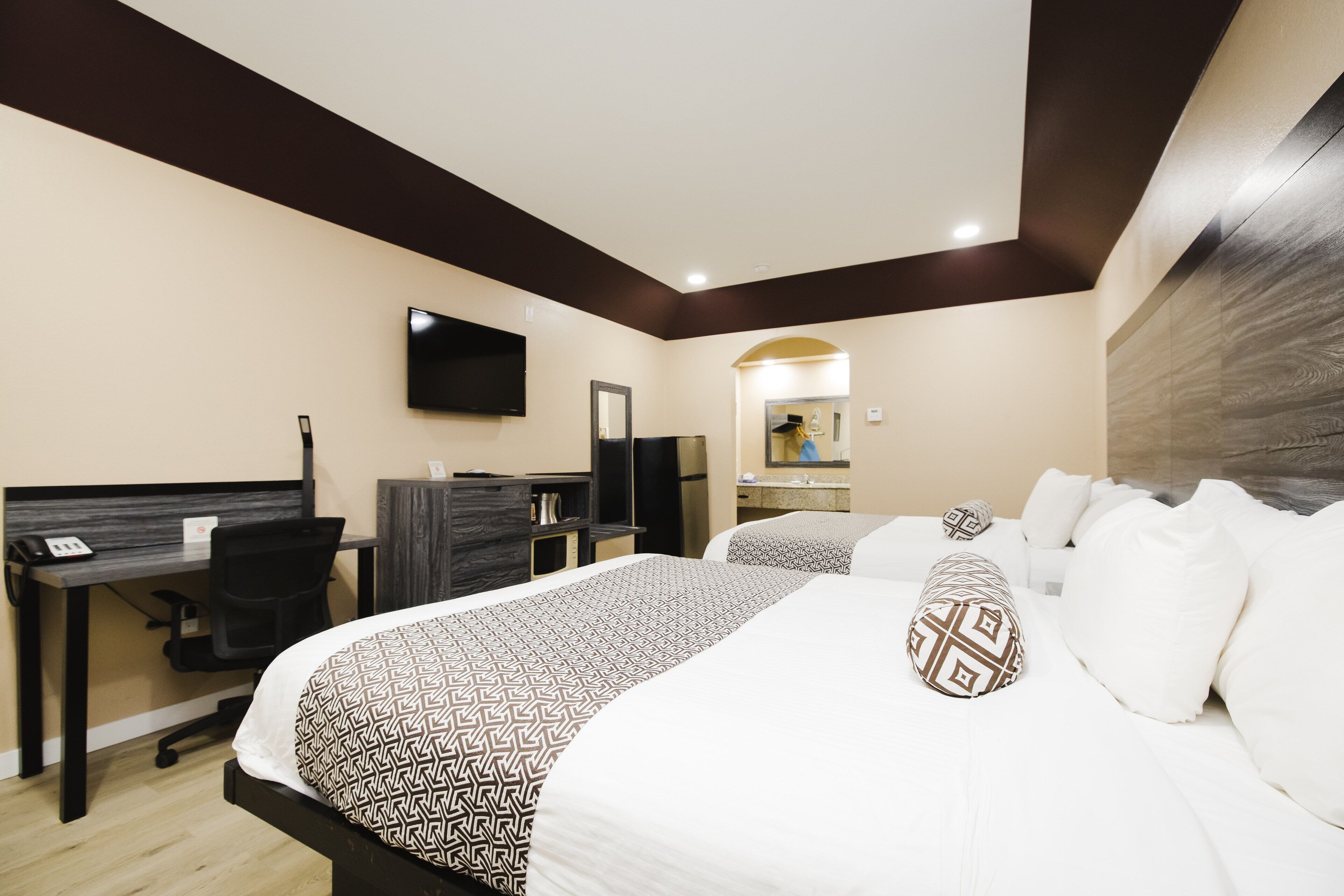 Quarto de hotel com uma cama grande, uma escrivaninha, uma cadeira, uma televisão e um espelho.