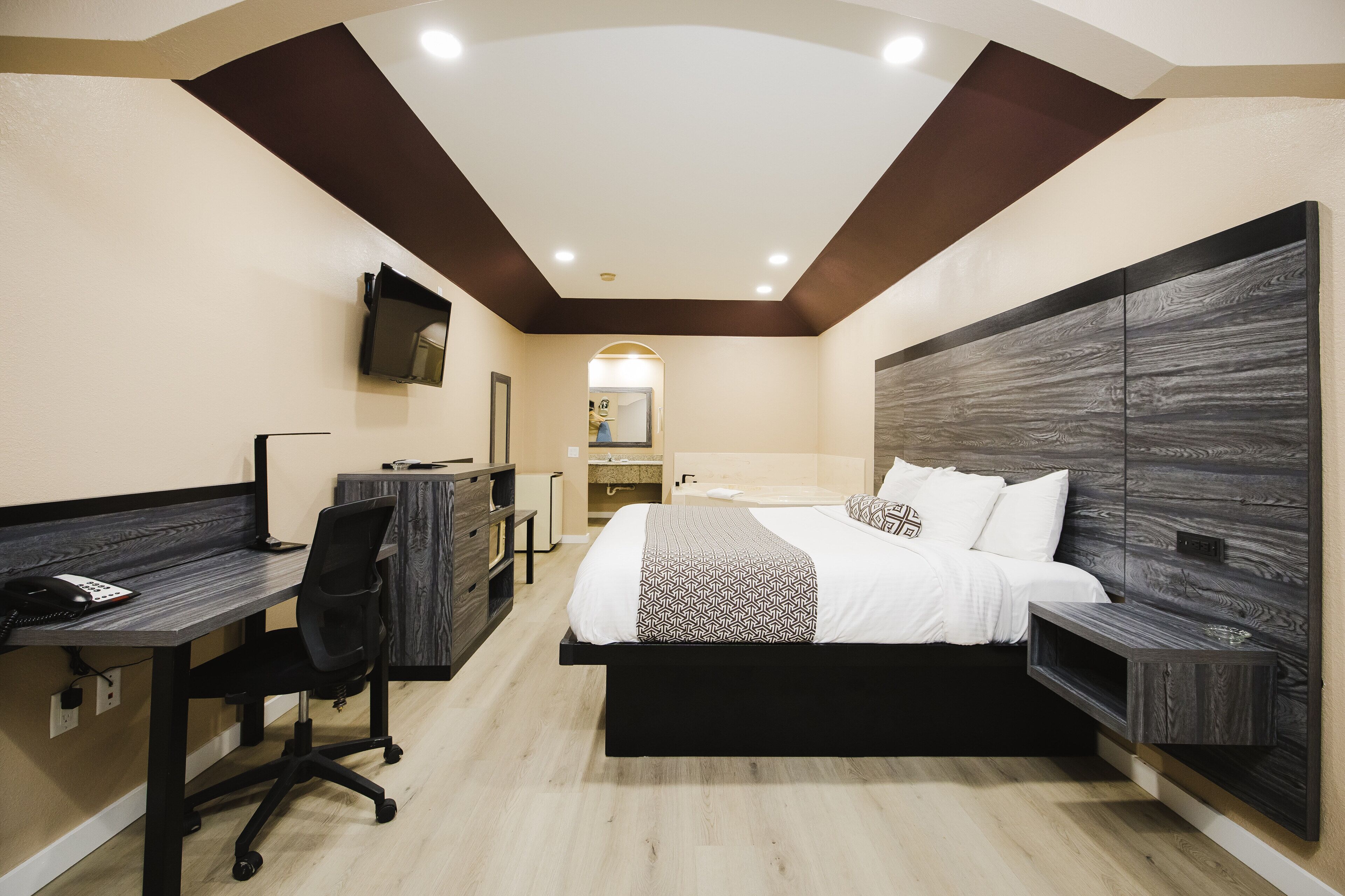 Quarto moderno com cama, escrivaninha e cadeira, com TV integrada e toucador com espelho.