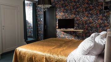 Quarto com cama, televisão na parede e papel de parede floral.