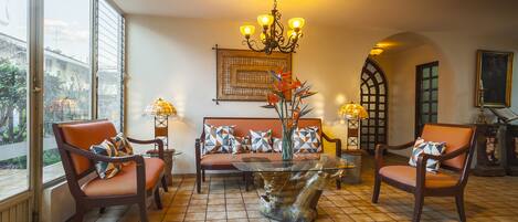 Uma sala de estar ampla com uma mesa de centro de vidro, duas poltronas, um sofá e um candelabro.