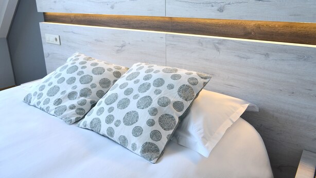 Cama com roupa de cama branca e duas almofadas com padrão circular cinza e branco.
