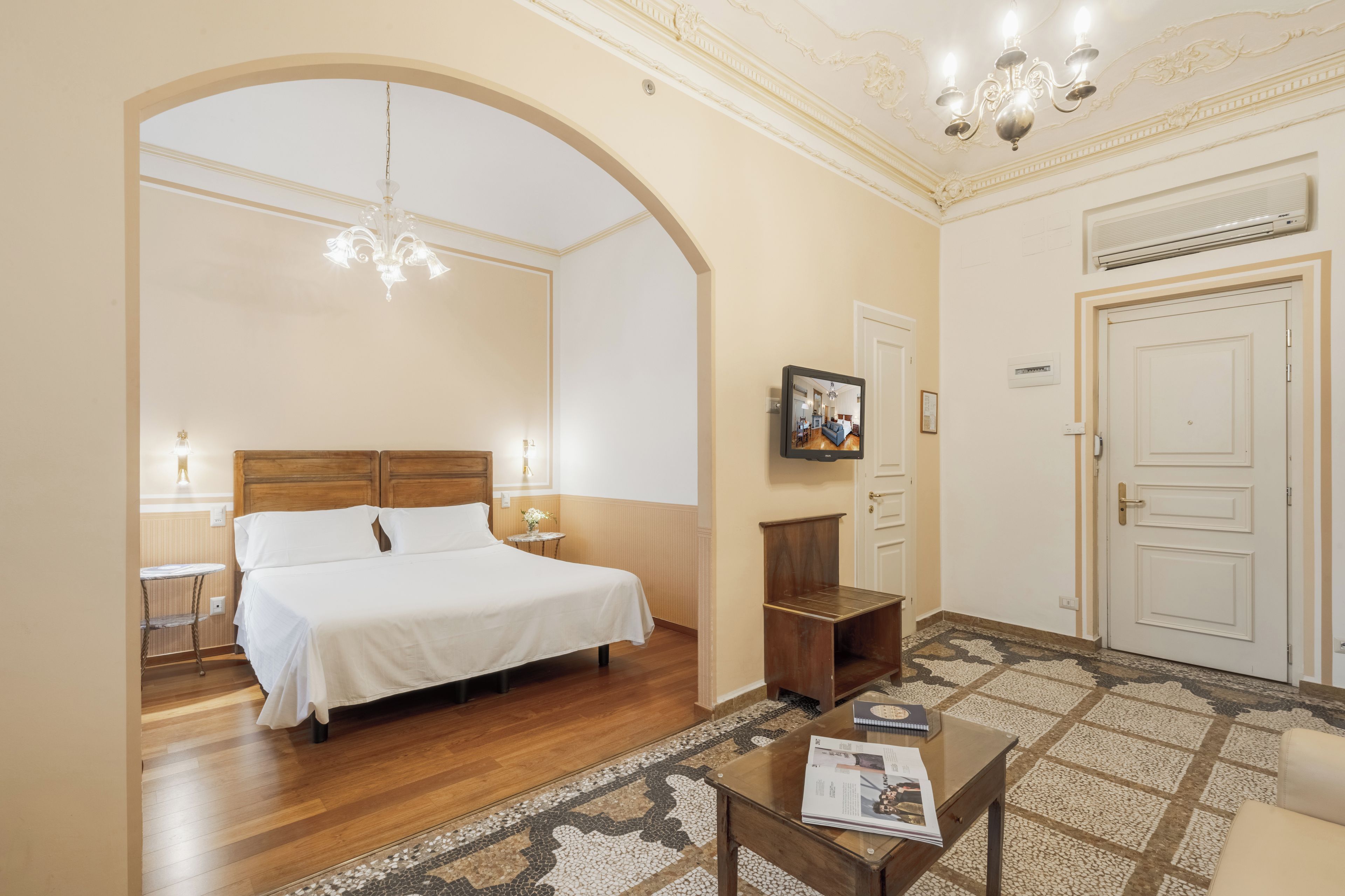 Quarto de hotel com uma cama grande, uma mesa pequena, uma cadeira, um espelho e uma porta.