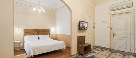 Quarto de hotel com uma cama grande, uma mesa pequena, uma cadeira, um espelho e uma porta.