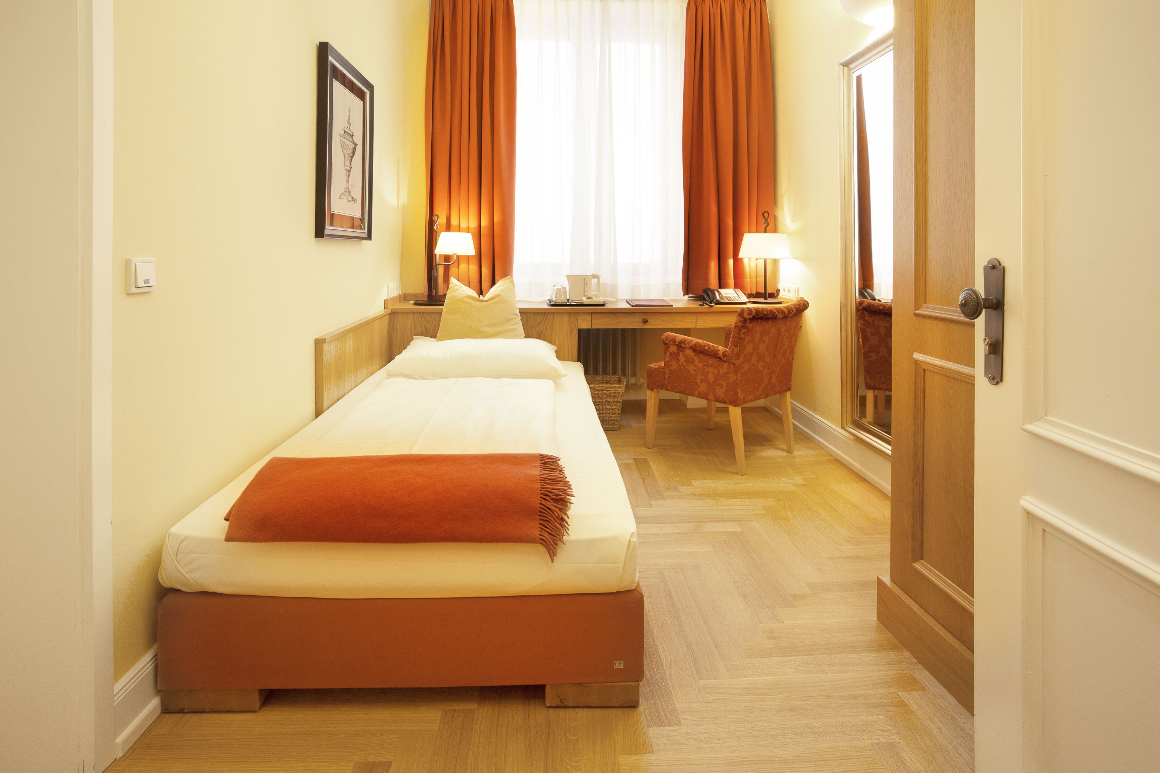 Quarto de hotel com cama, escrivaninha, cadeira e porta.