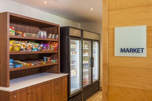 Uma área de mercado com prateleiras repletas de lanches e um refrigerador com produtos.