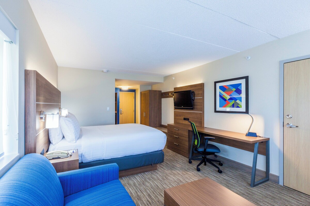 Quarto de hotel com uma cama, uma escrivaninha, uma cadeira, um sofá e uma porta.