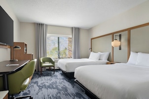 Quarto de hotel com duas camas, uma escrivaninha, uma cadeira, uma televisão e uma janela com cortinas.