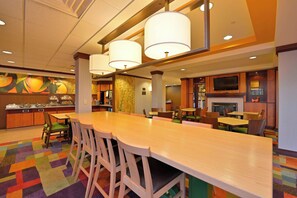 Um lobby de hotel com um longo balcão de recepção de madeira, várias áreas de estar e uma televisão fixada na parede.