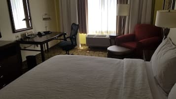 Quarto de hotel com cama, escrivaninha, cadeira, poltrona vermelha e abajur.