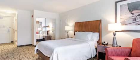 Quarto de hotel com cama, mesa de cabeceira, abajur, cadeira e um quadro na parede.