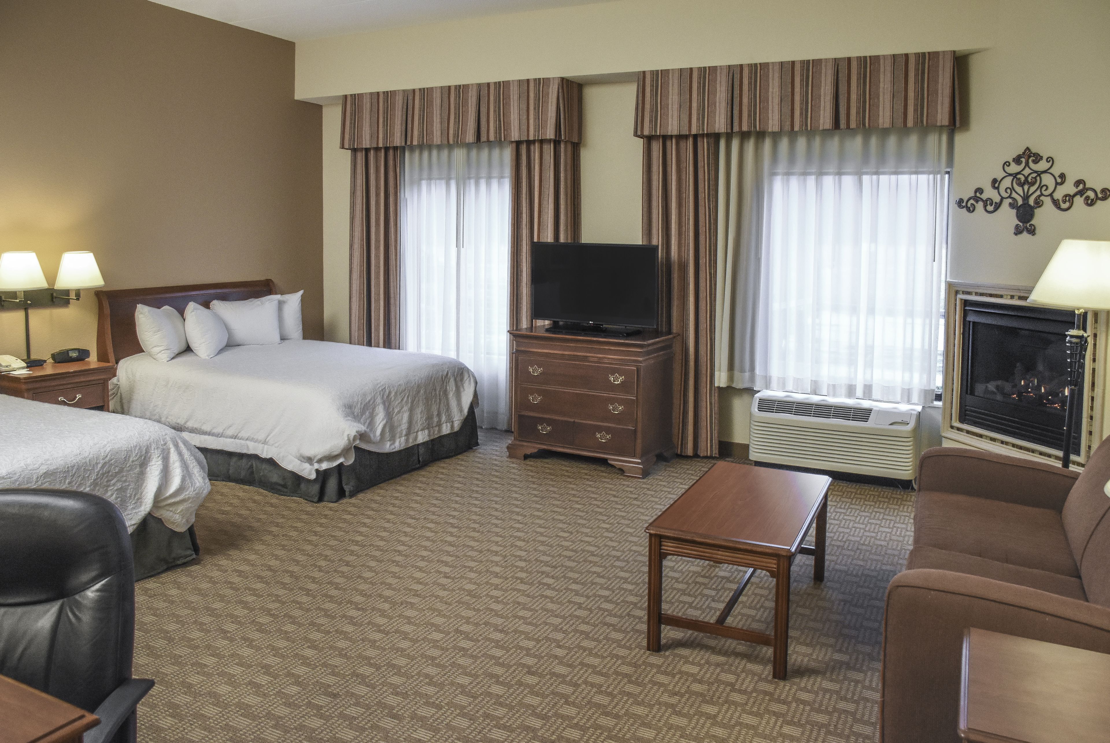Quarto de hotel com duas camas, televisão, lareira e uma escrivaninha.