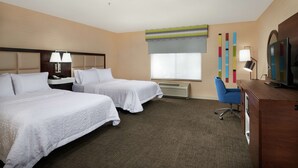 Quarto de hotel com duas camas, uma mesa, uma cadeira, televisão e janela com vista.