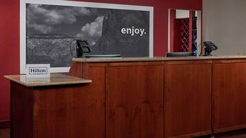 Balcão de recepção de hotel com um grande cartaz de uma paisagem montanhosa e a palavra 'enjoy' na parede.