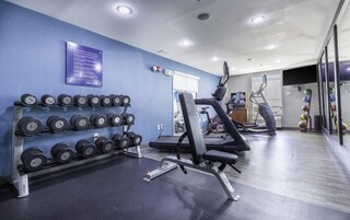 Uma academia com equipamentos de ginástica, uma placa na parede com regras de uso e uma janela com vista para o exterior.