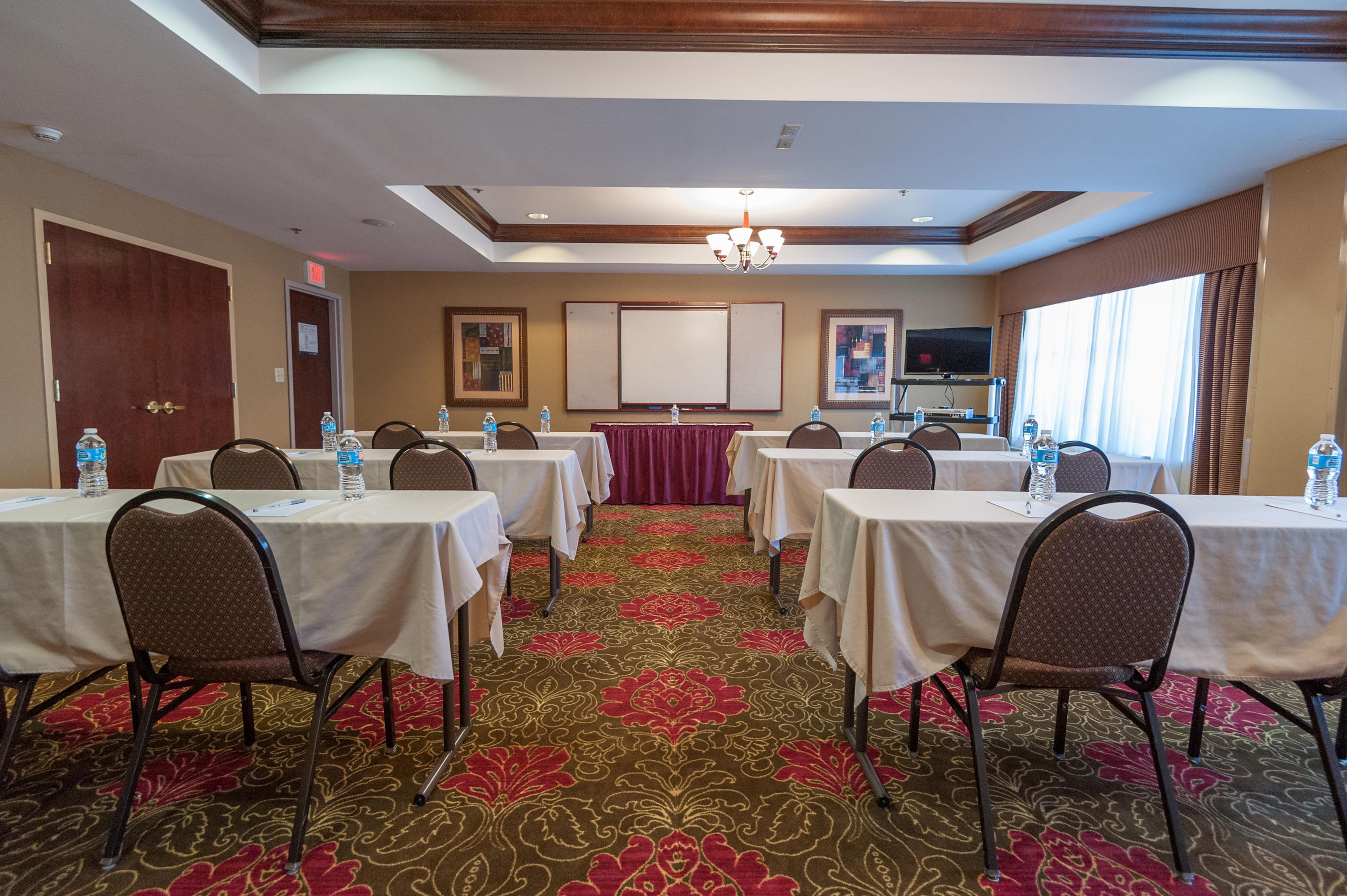 Sala de conferência com várias mesas e cadeiras, um candelabro e uma grande janela com cortinas.