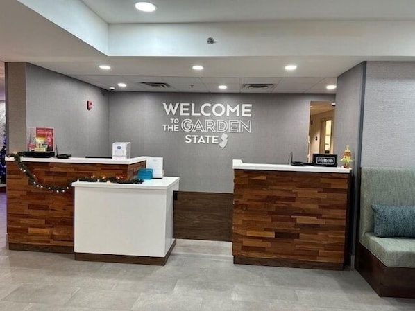 Uma área de recepção com uma placa 'Welcome to the Garden State', um balcão de atendimento, uma placa 'Hilton' e uma área de estar.