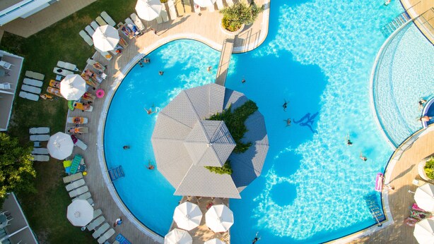 Uma piscina grande e curva com vários espreguiçadeiras e guarda-sóis ao redor.