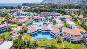 Vista aérea de um resort com vários edifícios, piscina central e áreas verdes ao redor.