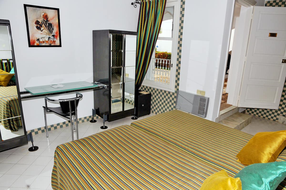 Quarto de hotel com cama, escrivaninha, cadeira, espelho e janela com cortinas.