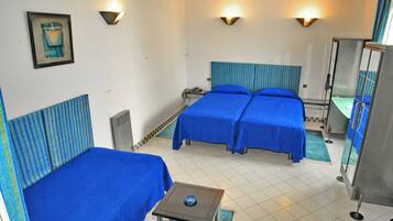 Quarto de hotel com duas camas, uma mesinha, um espelho e duas luzes fixadas na parede.