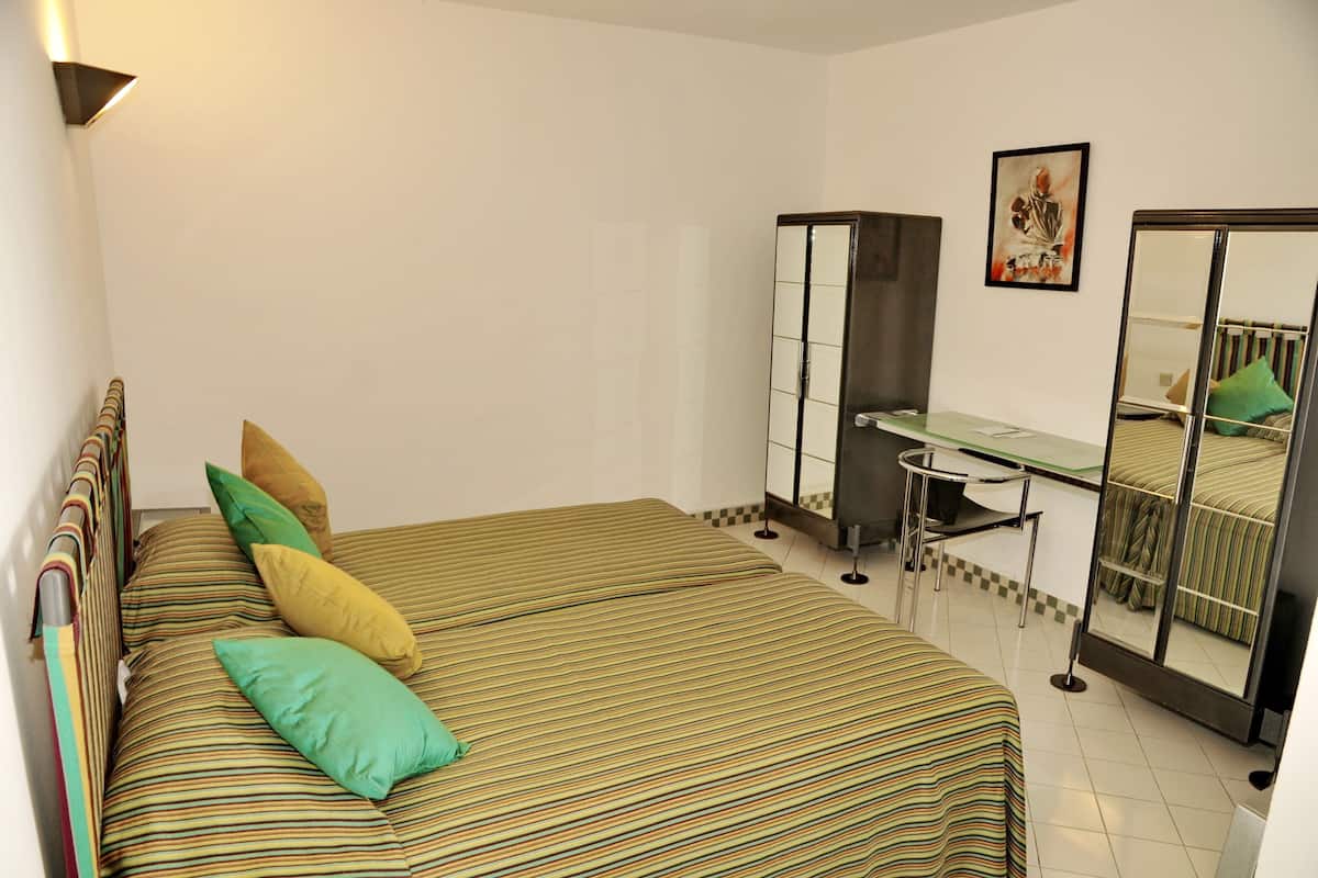 Quarto de hotel com cama, escrivaninha e espelho.