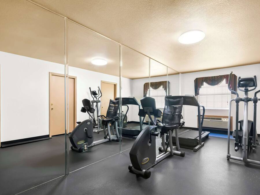 Uma academia com equipamentos de ginástica, um espelho grande e uma janela com cortinas.