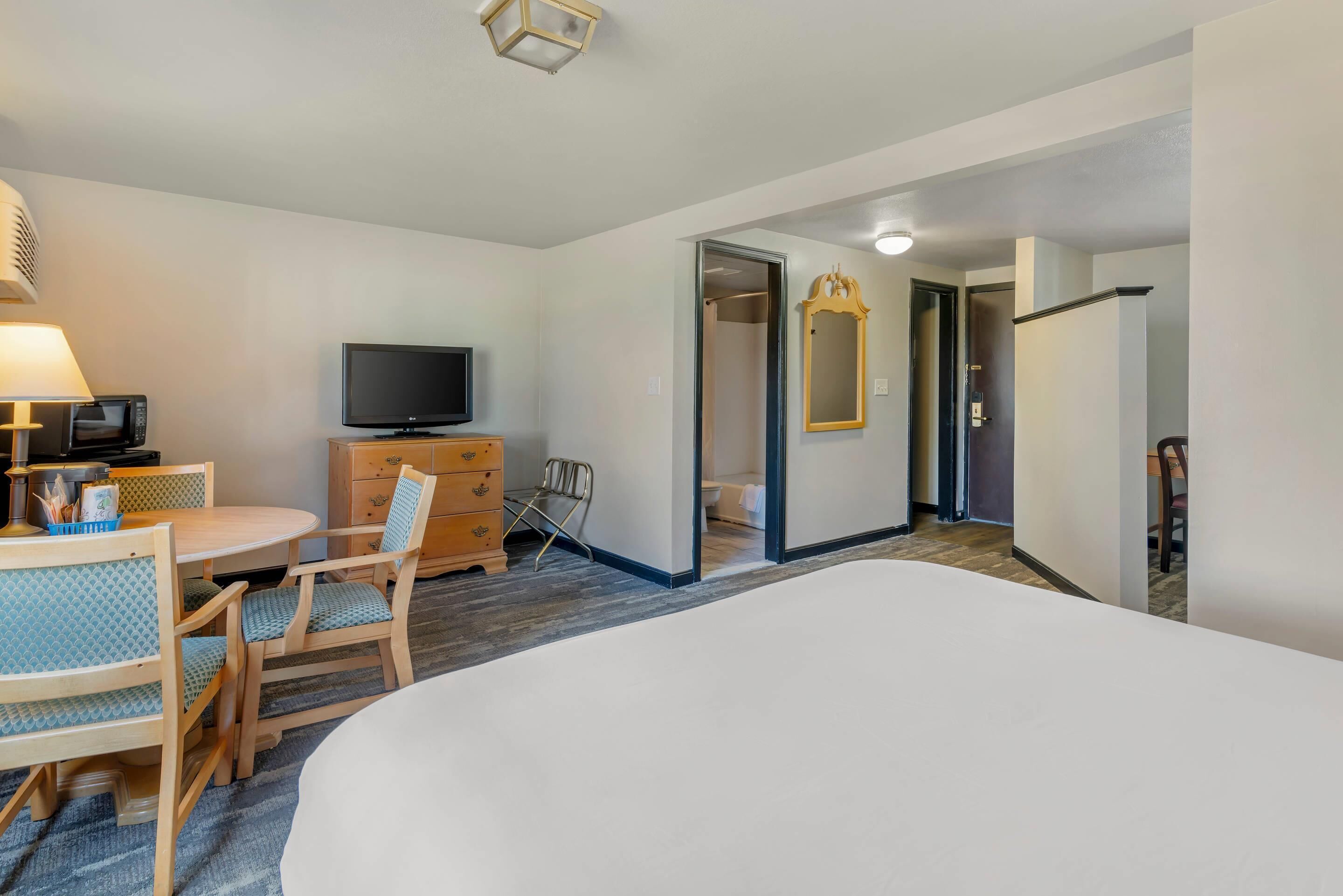 Quarto de hotel com cama, televisão, escrivaninha com cadeira, cômoda e espelho.