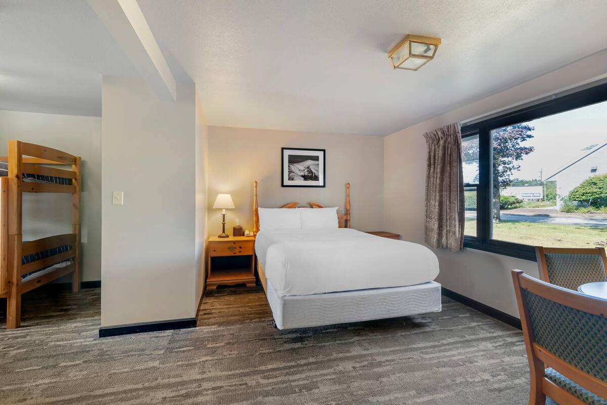 Quarto de hotel com cama, mesa de cabeceira, luminária e janela com vista.