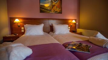 Quarto de hotel com duas camas, um quadro na parede e duas luminárias de cabeceira.