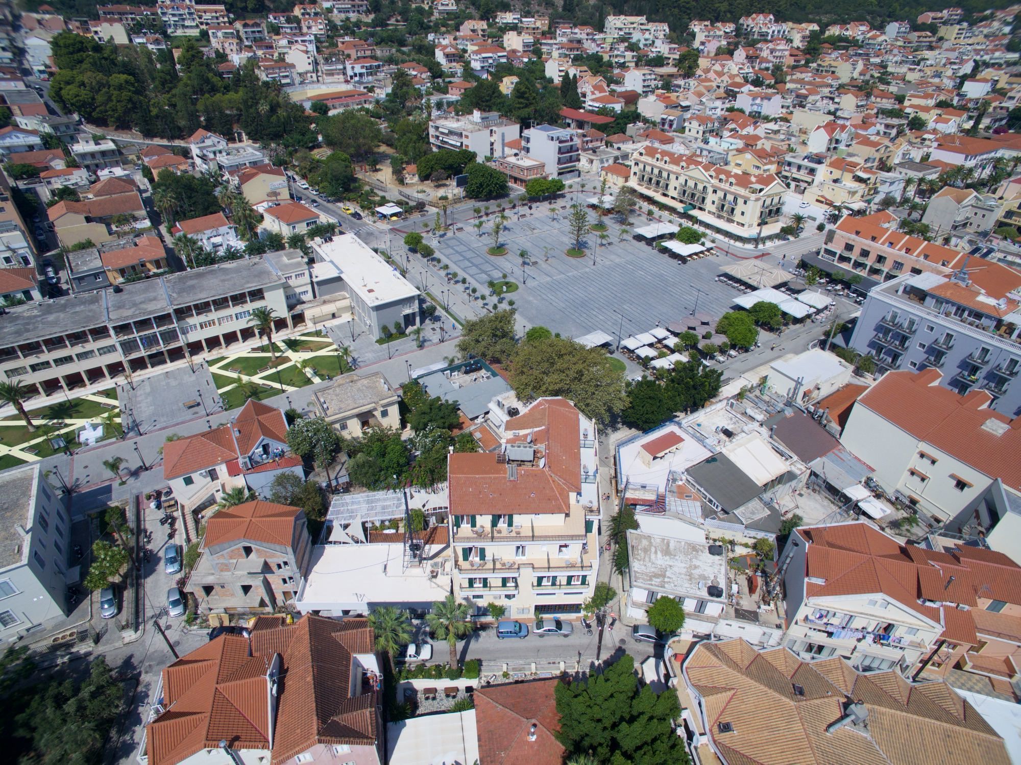 Vista aérea de uma área urbana densamente povoada, com edifícios residenciais e comerciais, destacando uma praça central com uma fonte, rodeada por ruas e carros estacionados.