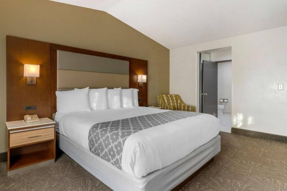 Quarto de hotel com uma cama grande, mesas de cabeceira, uma escrivaninha e uma cadeira.