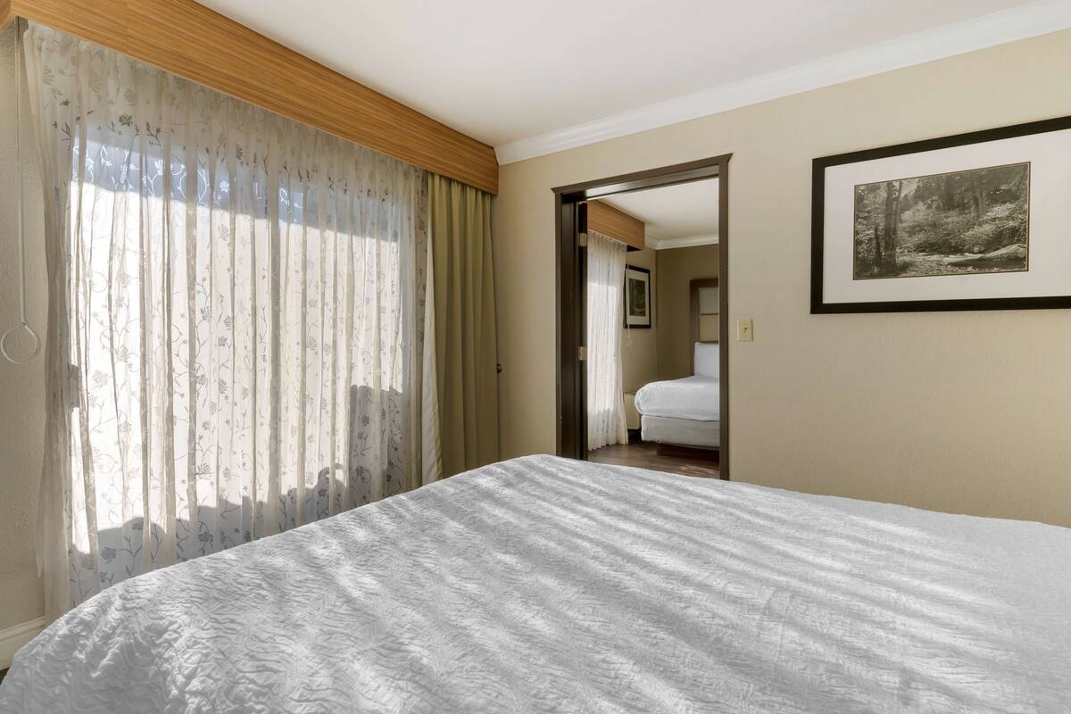 Quarto de hotel com uma cama grande, teto de madeira, quadro emoldurado na parede e vista através de uma porta aberta.