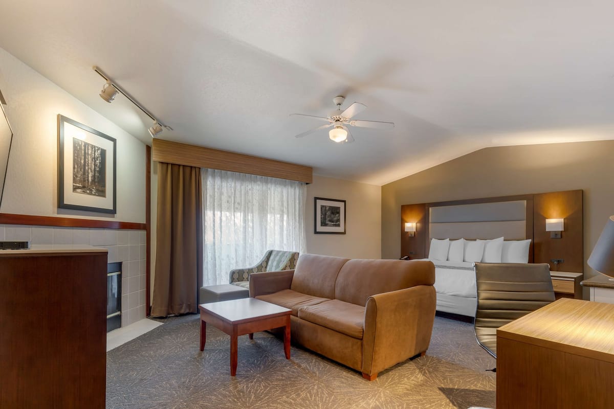 Quarto de hotel com cama, sofá, escrivaninha, cadeira, ventoinha no teto e lareira.