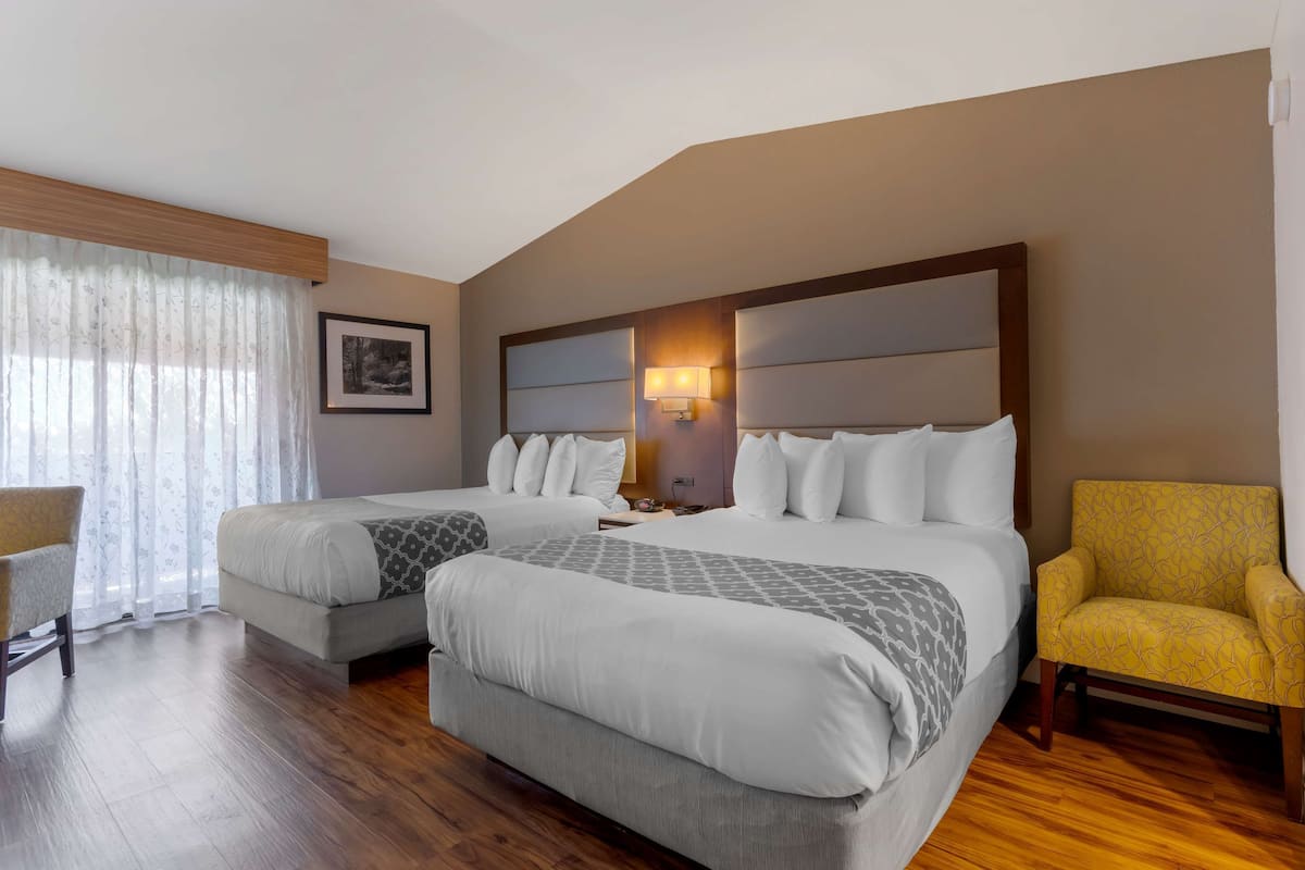 Quarto de hotel com duas camas, uma cadeira, um abajur e um quadro na parede.