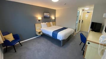 Quarto de hotel com cama, mesas de cabeceira, escrivaninha com telefone, uma cadeira e televisão.