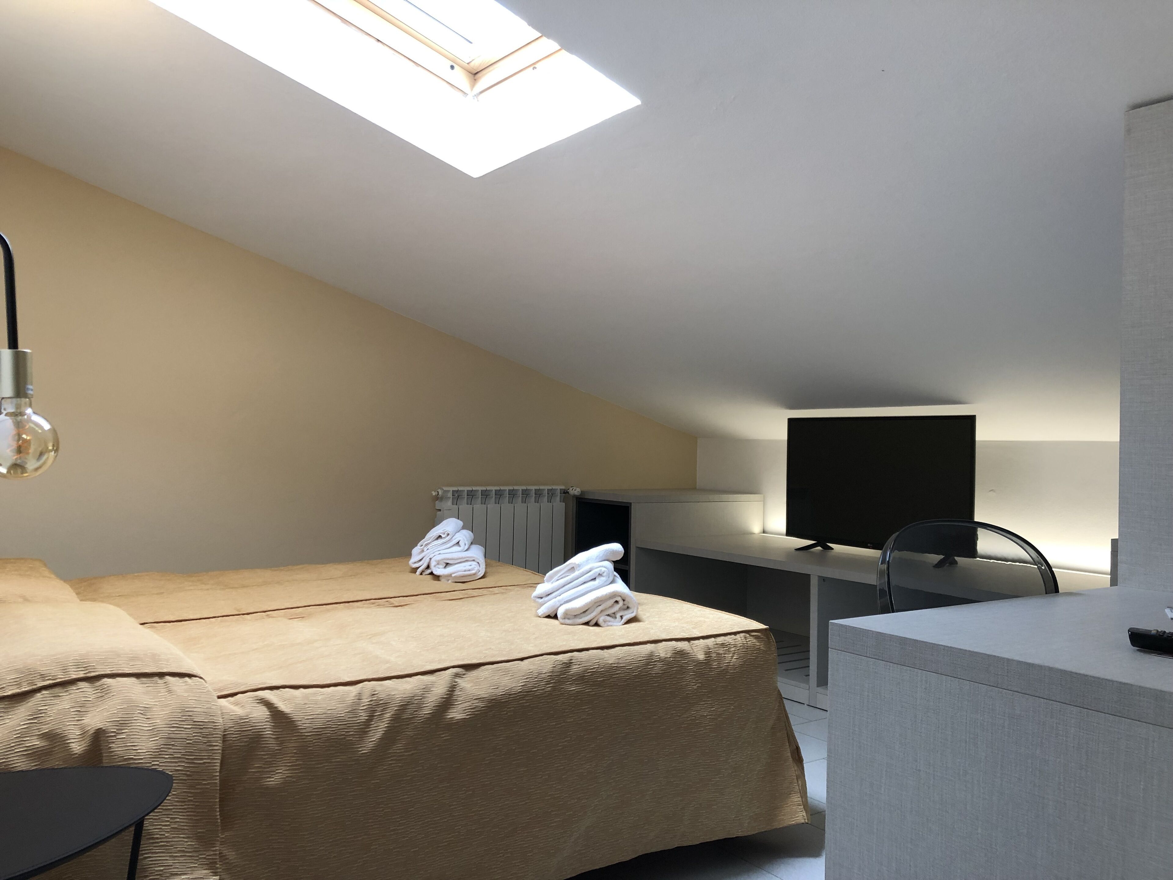 Um quarto moderno com claraboia, cama, escrivaninha e televisão.
