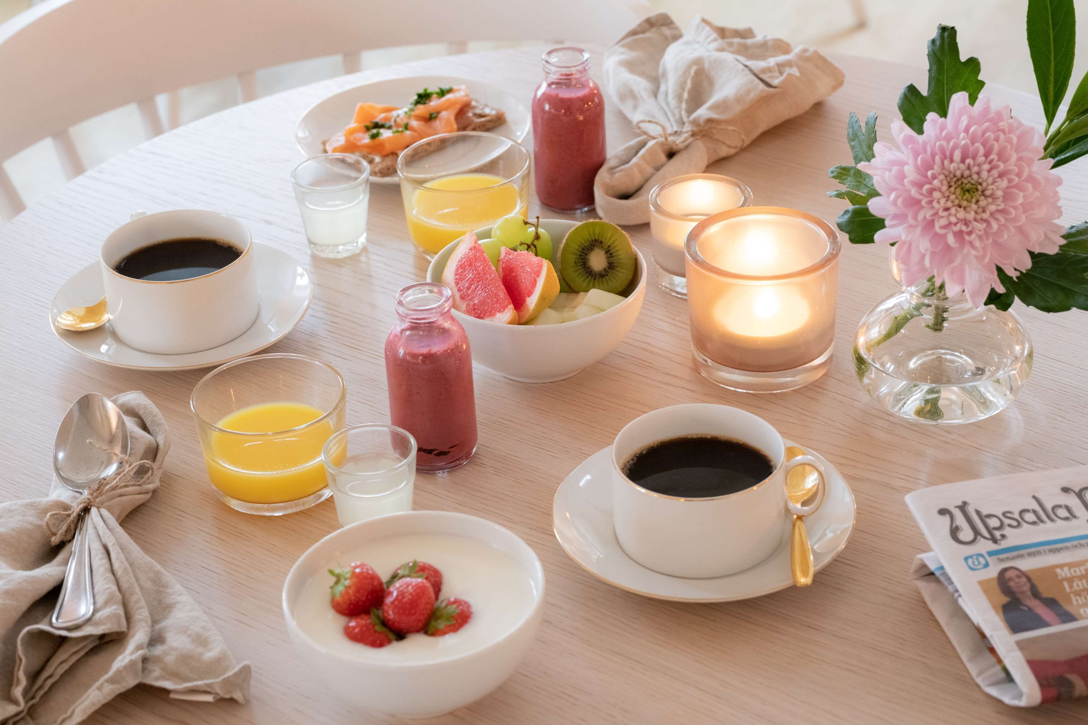Disposição de café da manhã com diversas bebidas, frutas e uma vela sobre a mesa.
